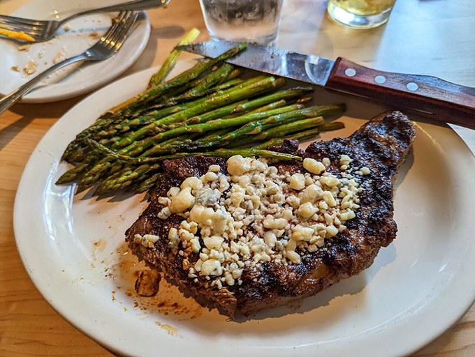The Black and Blue Ribeye arrives with blue cheese crumbles melting into the perfectly charred exterior, alongside asparagus that actually makes you want to eat vegetables.