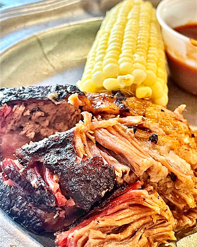 Behold the holy trinity: brisket with that perfect smoke ring, pulled pork with bark, and corn on the cob. A plate that silences conversation.