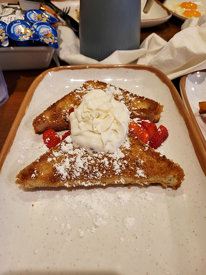 Two golden triangles of French toast perfection, dusted with powdered sugar and crowned with whipped cream like breakfast royalty deserves.