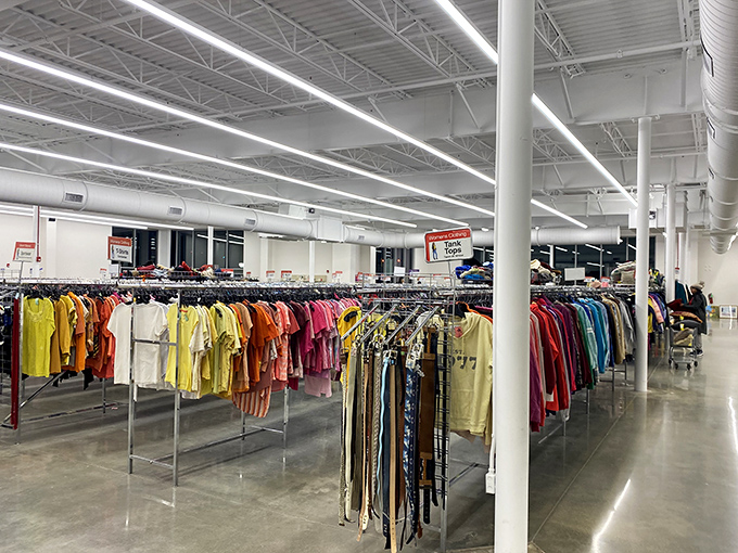 Color-coded clothing racks create a rainbow road of possibilities, where organization meets opportunity under bright industrial lighting.