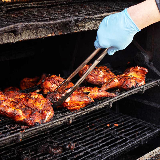 Tongs delicately lift chicken that's achieved barbecue nirvana &ndash; that perfect mahogany color that signals flavor has penetrated to the bone. Patience made visible.