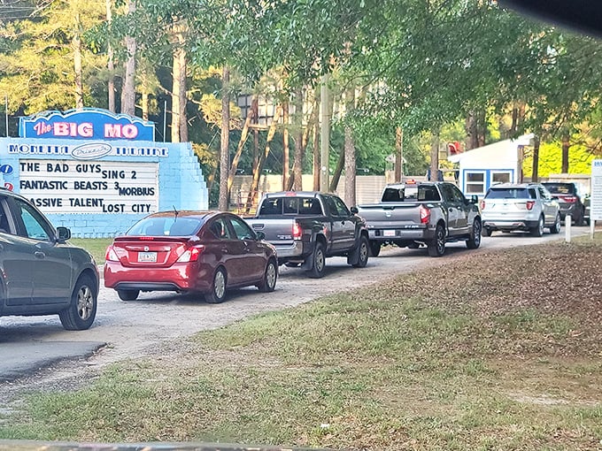 The entrance marquee announces tonight's features as cars queue up, each vehicle filled with anticipation and probably too many snacks.