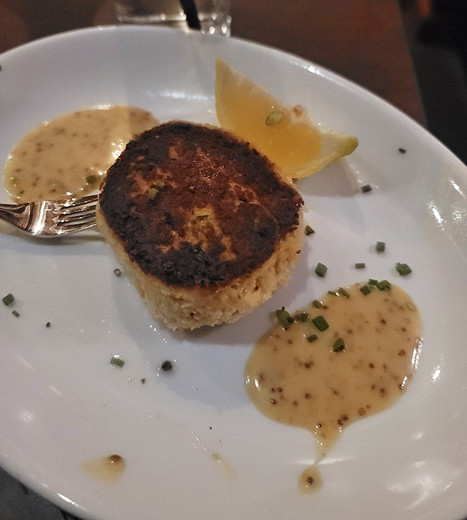 The Maryland Crab Cake arrives like a golden-brown island of pure crab joy, surrounded by a sea of remoulade that deserves its own zip code.
