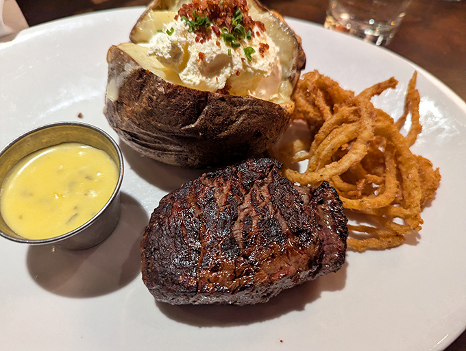 This filet mignon arrives like royalty with its perfectly charred exterior, accompanied by a loaded baked potato and crispy onion straws fit for its majesty.