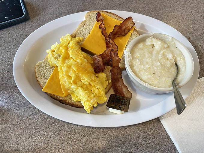 Breakfast perfection on a plate: fluffy scrambled eggs, crispy bacon, and a side of creamy grits that would make any Southerner nod in approval.