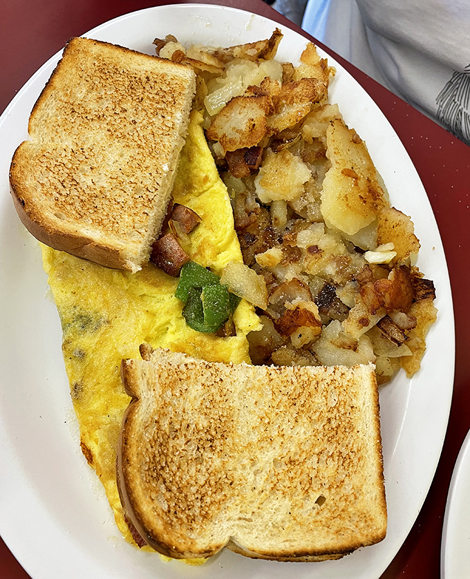Breakfast perfection on a plate - golden toast, a fluffy omelet studded with veggies, and home fries that make you question all other potatoes you've ever eaten.