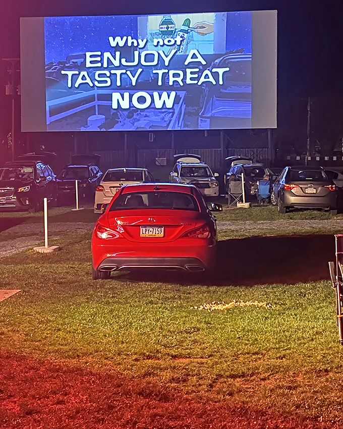 Cars gather under the night sky as the screen glows with tempting concession ads between features.