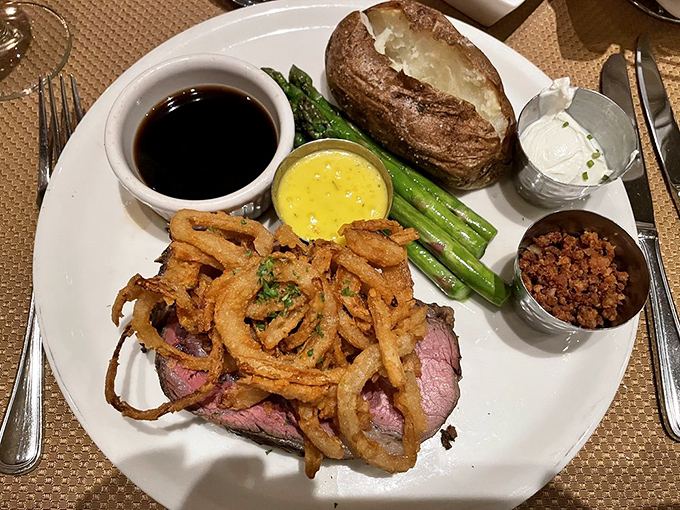 The star of the show arrives: prime rib adorned with crispy onions, accompanied by a loaded baked potato, asparagus, and the kind of au jus you'll be tempted to sip.