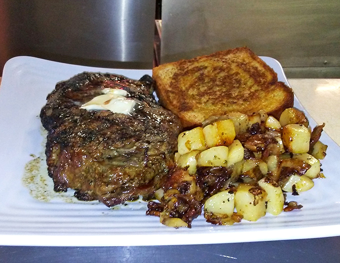 A perfectly seared ribeye with a pat of melting butter, golden toast, and home fries&mdash;proof that heaven exists on a white plate.