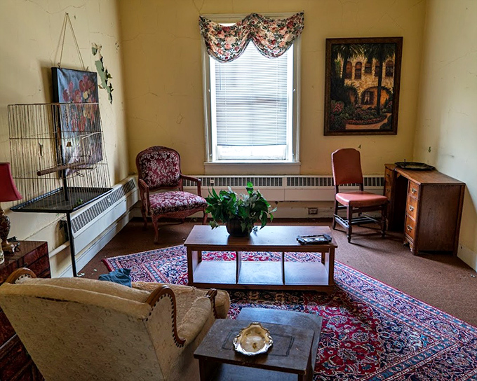 Someone's attempt at normalcy amid institutional walls. The floral curtains and vintage furniture create an unsettling juxtaposition against the building's grim history.