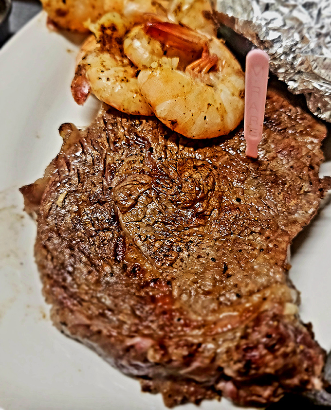 A perfectly seared ribeye with jumbo shrimp perched atop like a proud seafaring conquistador claiming new territory&mdash;surf and turf perfection.