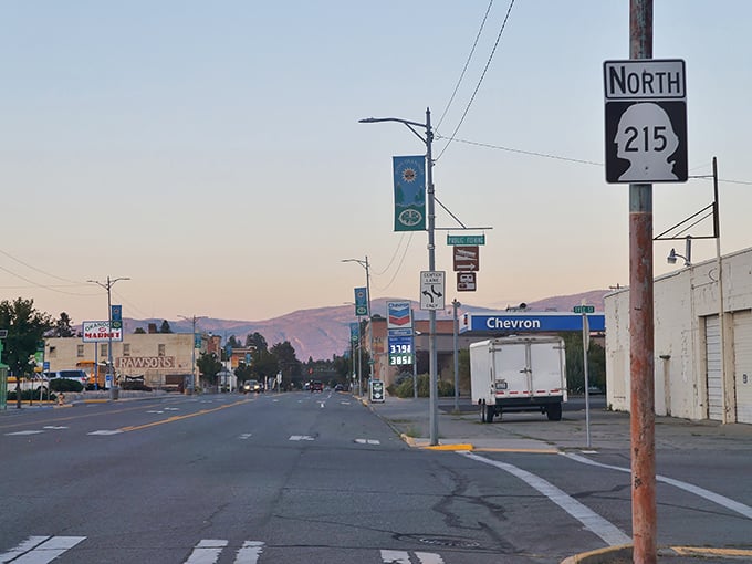 Twilight paints Omak's Chevron sign with golden hues as Highway 215 stretches toward purple mountain shadows.