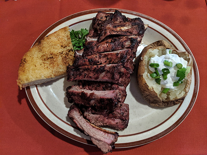 A symphony of textures on one plate: sliced steak with that signature oak-fired char, garlic bread for sopping, and a loaded baked potato.
