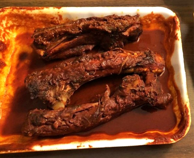 Beef ribs lounging in their sauce bath like they're at a five-star spa. The meat's already surrendering from the bone.