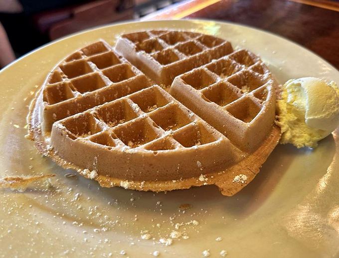 This Belgian waffle isn't just breakfast, it's architecture—perfectly formed squares waiting to become swimming pools for maple syrup and melting butter.