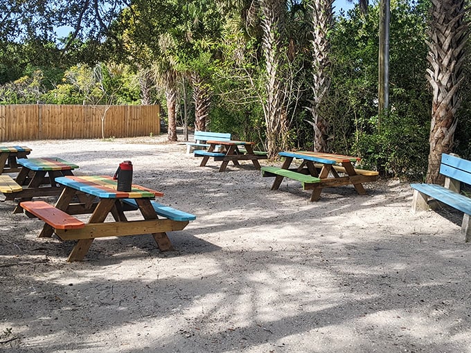 Colorful picnic tables await hungry beachgoers. Someone clearly got the memo that dining al fresco tastes better when your table matches your tropical shirt.