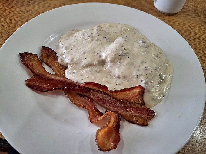 This isn't just biscuits and gravy &ndash; it's a warm blanket of peppery comfort atop fluffy biscuit clouds, with bacon standing by for moral support.