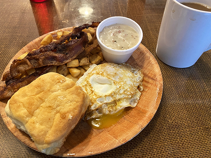 Breakfast perfection on a wooden plate: a sunny-side-up egg, golden biscuit, and crispy bacon&mdash;the holy trinity of morning happiness.