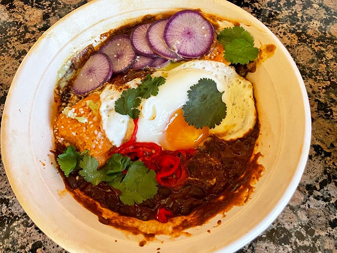 This breakfast tamale redefines morning expectations—a beautiful chaos of stewed black beans, cilantro crema, and that perfect sunny egg on top.
