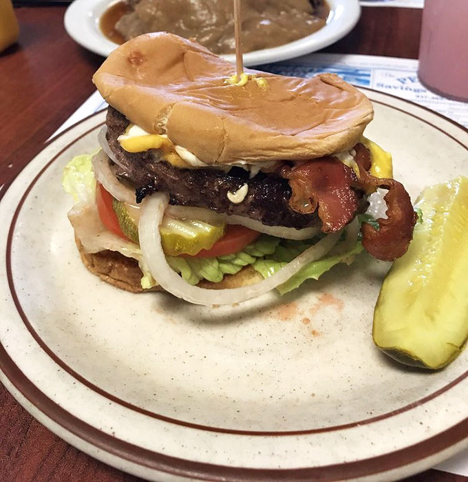 A burger that requires both hands and your full attention. That pickle spear isn't just garnish&mdash;it's the perfect palate cleanser between bites.
