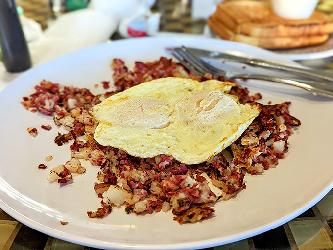 Corned beef hash topped with a perfect sunny-side-up egg – breakfast architecture at its finest. The crispy-to-soft ratio is mathematical perfection.