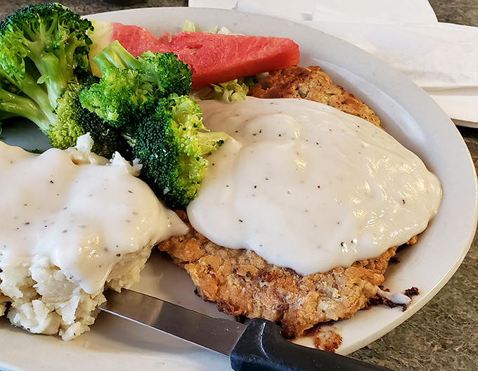 Country-fried steak wearing its gravy like a tailored suit, accompanied by vegetables pretending you're making healthy choices. Spoiler alert: you're not, and that's okay.