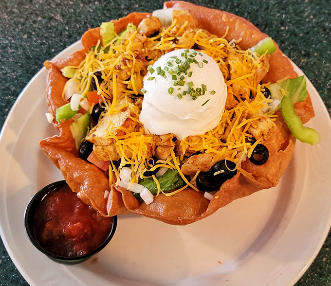 The chicken taco salad arrives like edible architecture&mdash;a crispy tortilla bowl cradling seasoned chicken, cheese, and veggies, crowned with a dollop of sour cream.