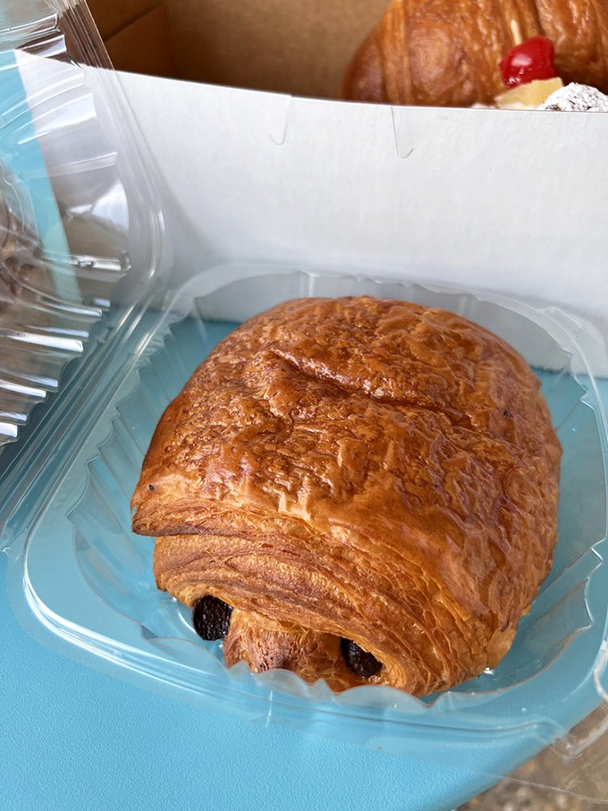 The chocolate croissant flaunts its perfect layers like a supermodel on a runway, with chocolate peeking out just enough to make promises it fully intends to keep.