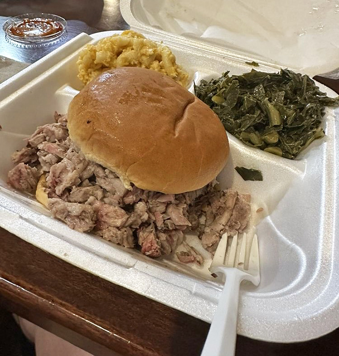 A chopped pork sandwich so generous it's practically spilling over, with collard greens and mac and cheese standing by as worthy companions.