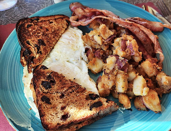 Breakfast perfection on a turquoise plate: crispy toast, golden eggs, home fries that crackle with flavor, and bacon that means business.