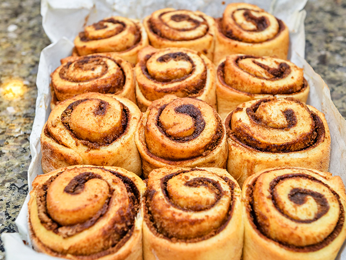 Fresh cinnamon rolls lined up like sweet soldiers awaiting their caramel bath. Resistance is futile, surrender is delicious.