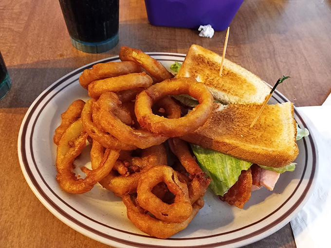 The onion rings form a golden fortress around a sandwich that's dressed better than most people at church on Sunday.