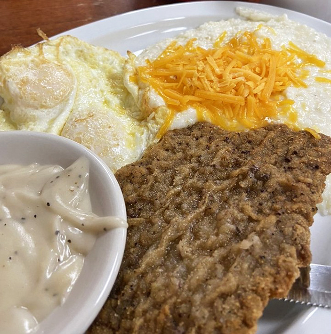 The holy trinity of breakfast: country fried steak, eggs with cheese, and gravy. A plate that says "good morning" like a warm hug.