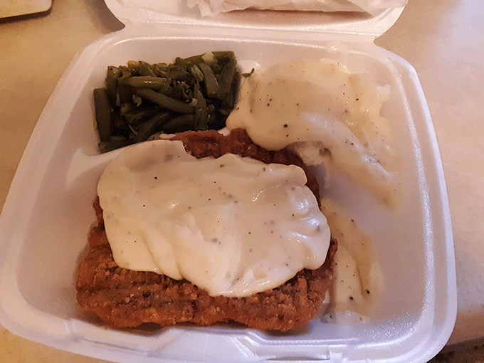 The chicken fried steak arrives smothered in creamy white gravy like a warm blanket on a cold day, with green beans offering a token vegetable presence.