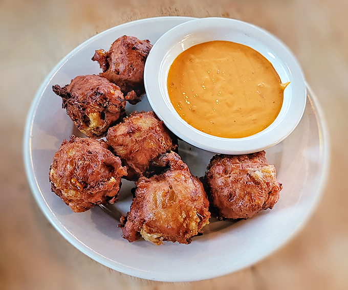 These crab fritters arrive like little golden orbs of joy, accompanied by a dipping sauce that demands to be savored.