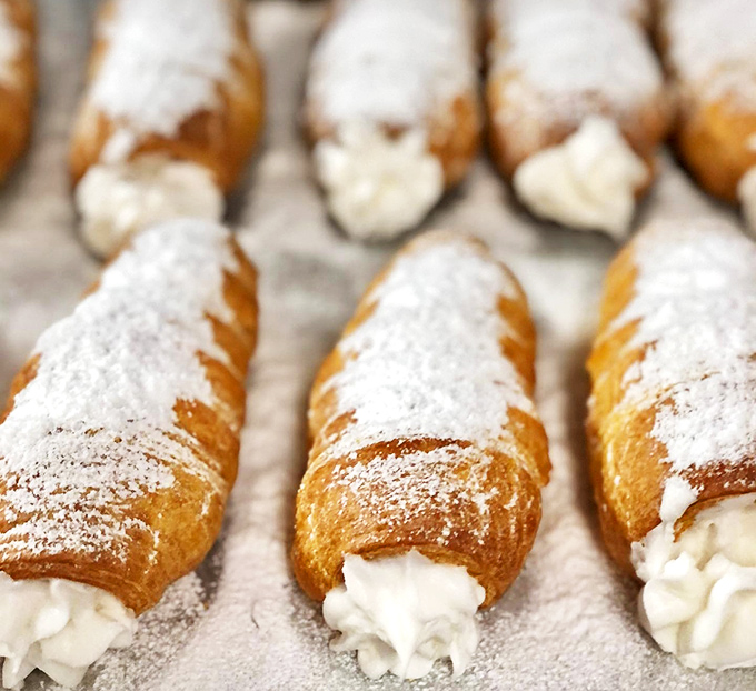 Cream horns lined up like delicate instruments in a sugar orchestra, their powdered exteriors hiding the silky treasure within.