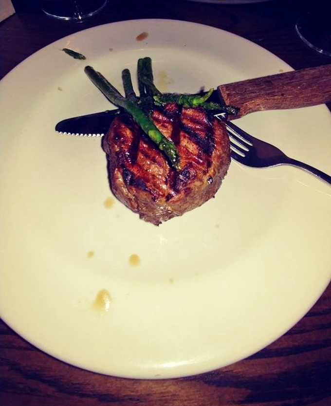 The filet mignon arrives like a meaty monument to perfection, topped with asparagus spears standing at attention like they know they're in the presence of greatness.
