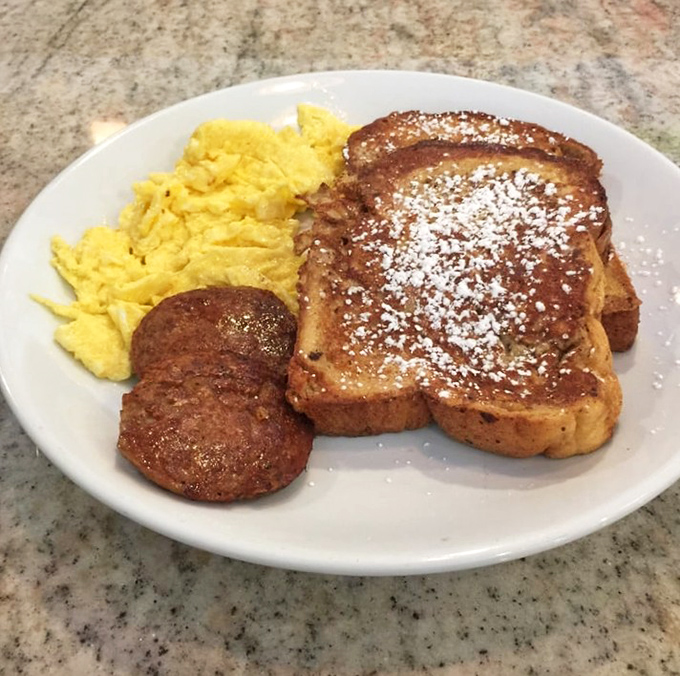 French toast dusted with powdered sugar alongside scrambled eggs and sausage—the breakfast equivalent of a greatest hits album on a plate.