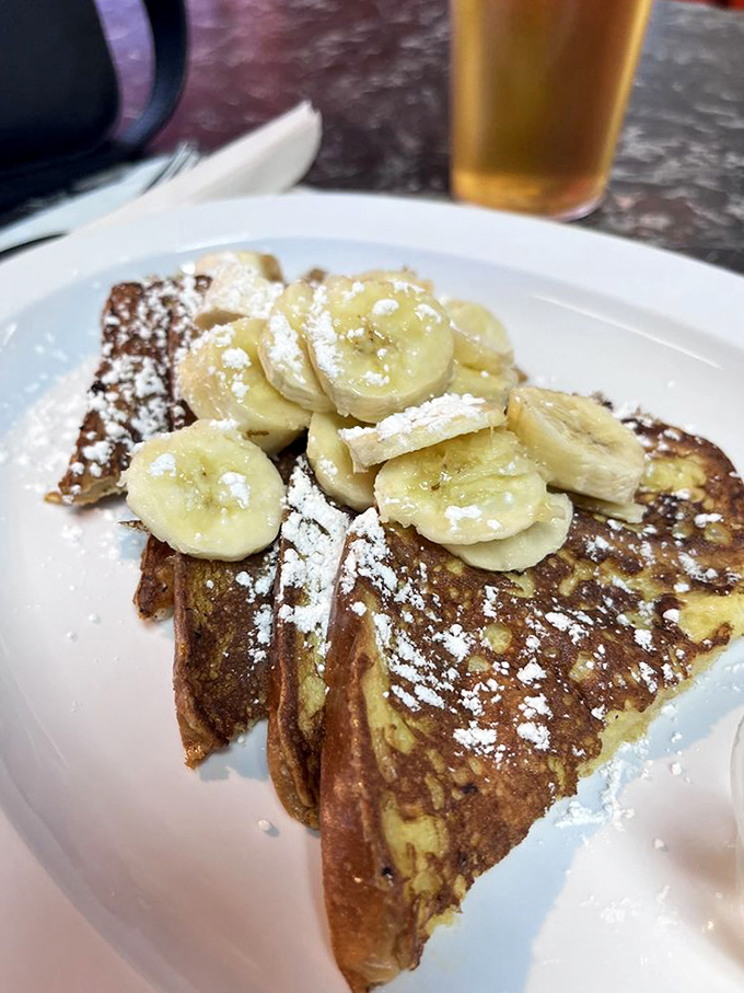 French toast that justifies the hype! Golden-brown perfection topped with fresh bananas and a snowfall of powdered sugar. Worth every calorie.