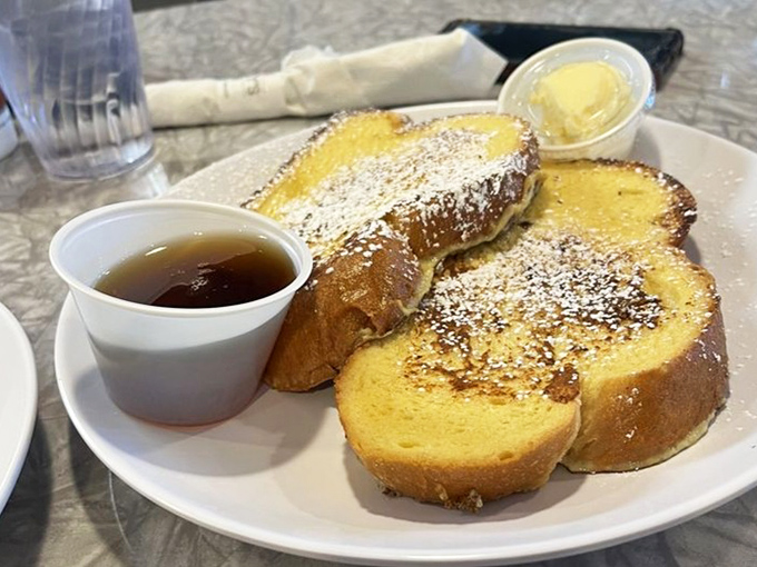 French toast that's dressed for success with a dusting of powdered sugar. The syrup cup stands by, ready for its supporting role.