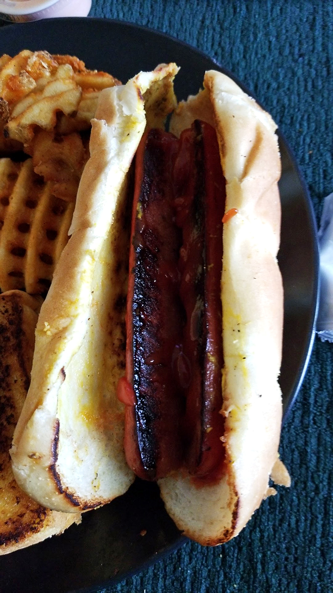 That hot dog knows how to make an entrance, nestled perfectly in its toasted throne with waffle fries standing guard.