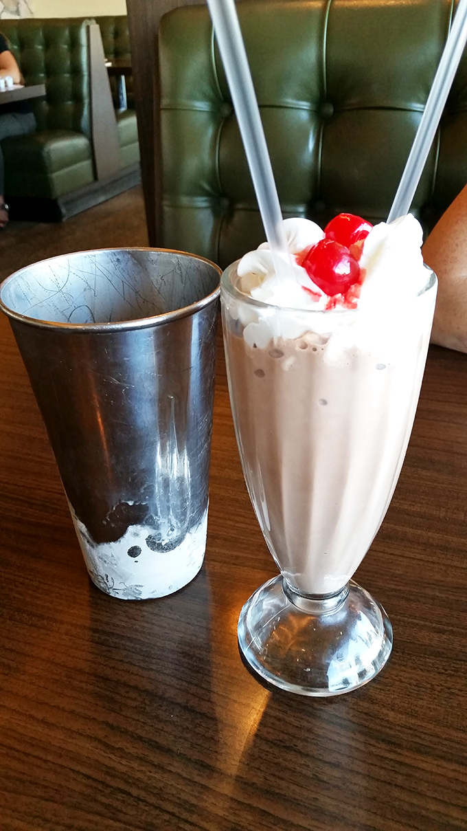 The milkshake arrives like a creamy tower of nostalgia, topped with whipped cream islands and cherry beacons&mdash;spoons and straws standing ready for the dairy expedition.