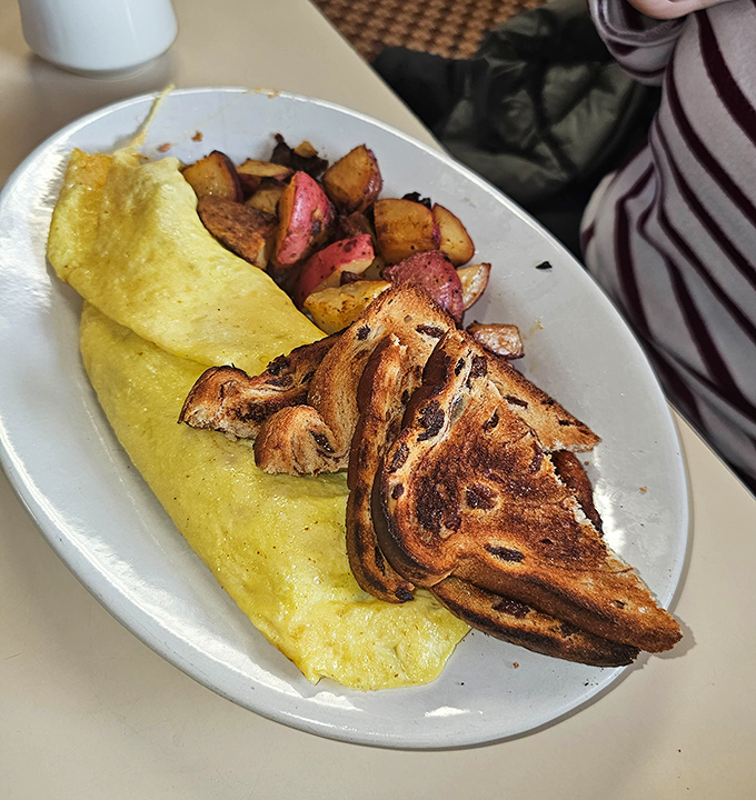 A perfectly executed omelet alongside marble rye and those legendary home fries &ndash; the holy trinity of diner breakfast excellence.