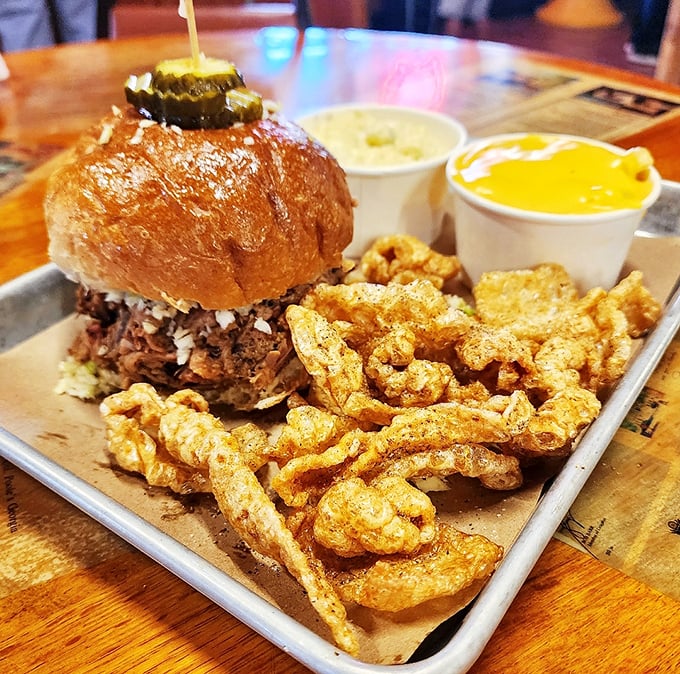 A pulled pork sandwich that doesn't need fancy frills, just a pickle crown and crispy pork rinds standing guard like delicious sentinels.