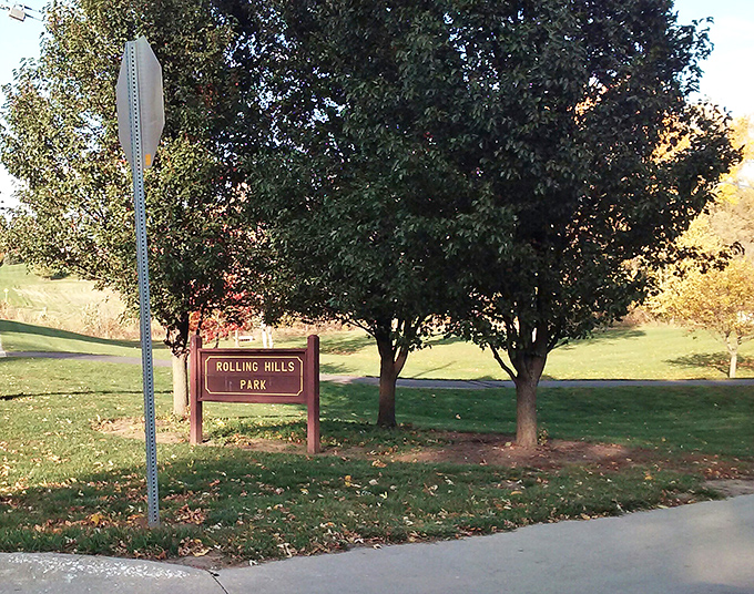 Rolling Hills Park lives up to its name with gentle slopes and mature trees. The sign promises exactly what it delivers&mdash;a peaceful green space without admission fees or parking hassles.