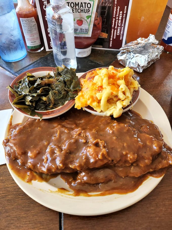 Smothered porkchop swimming in gravy alongside collard greens and mac & cheese&mdash;a holy trinity of comfort that makes Monday feel like Saturday.