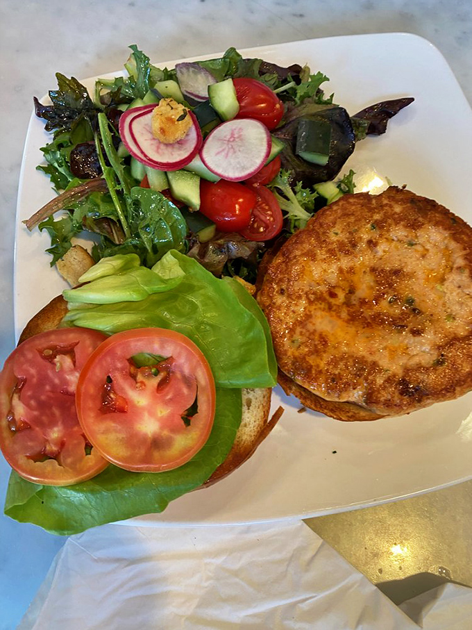 The Spicy Salmon Burger arrives like a California dream&mdash;golden-crisp exterior, vibrant salad companions, and a promise of ocean-fresh flavor in every bite.