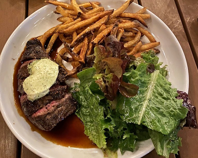 A perfectly cooked hanger steak with a pat of herb butter slowly melting into carnivorous bliss, accompanied by golden frites and fresh greens.