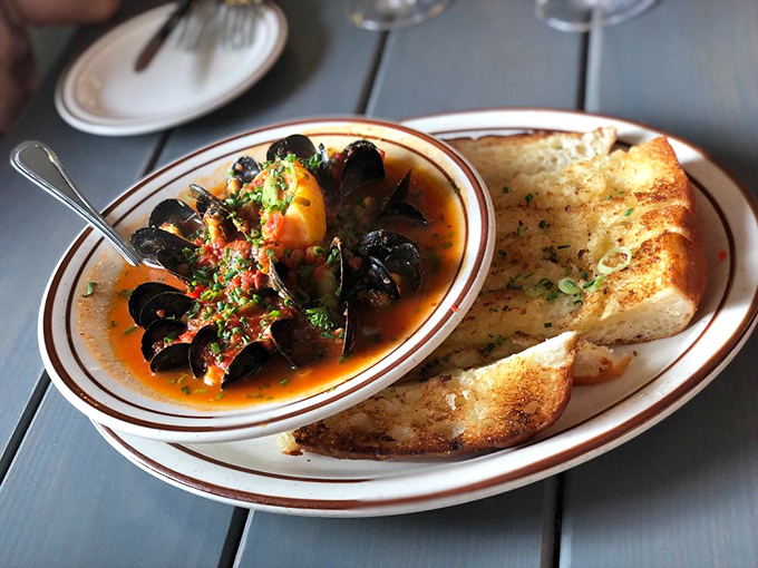 Steamed mussels swimming in a vibrant broth with grilled garlic bread standing by – nature's perfect tool for soaking up every last drop.