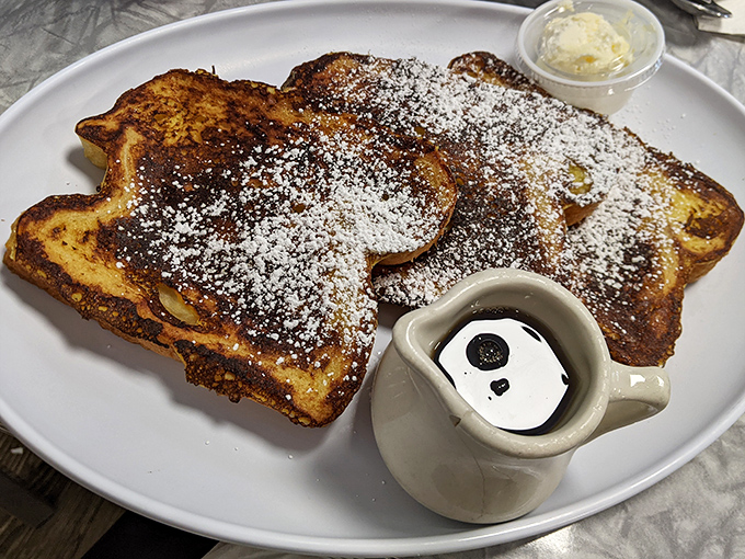 French toast that's dressed for success with a dusting of powdered sugar. The tiny pitcher of syrup stands ready for its grand moment.